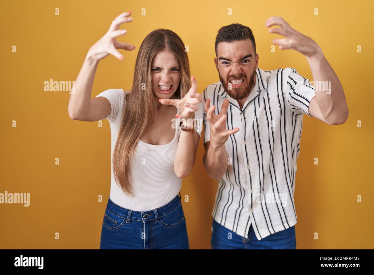 Young couple standing over yellow background shouting frustrated with ...