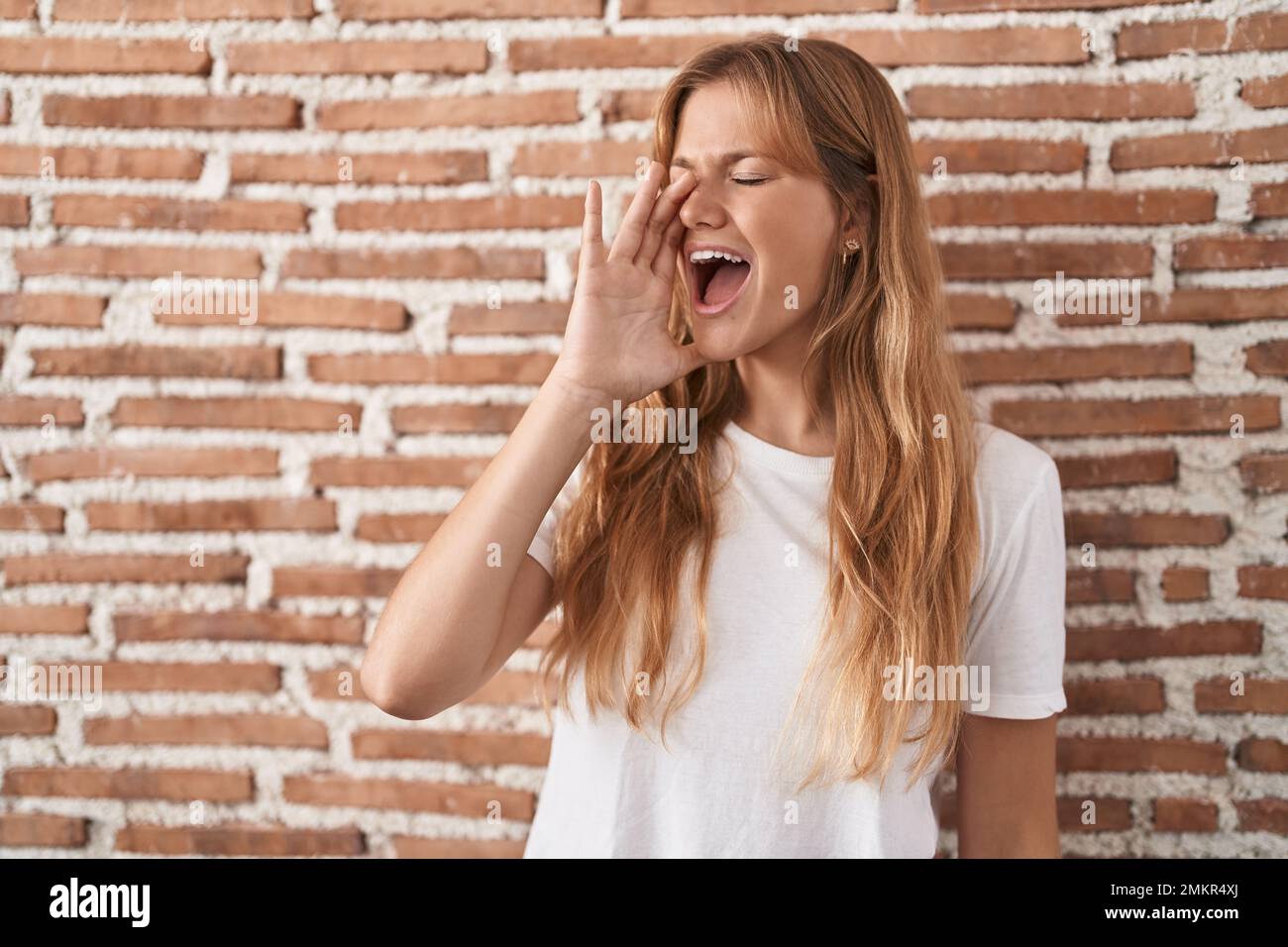 Young caucasian woman standing over bricks wall shouting and screaming ...