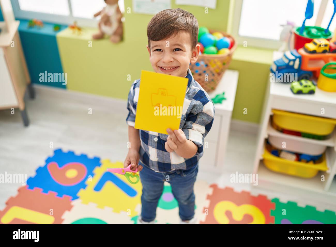 Adorable hispanic boy preschool student showing draw at kindergarten ...
