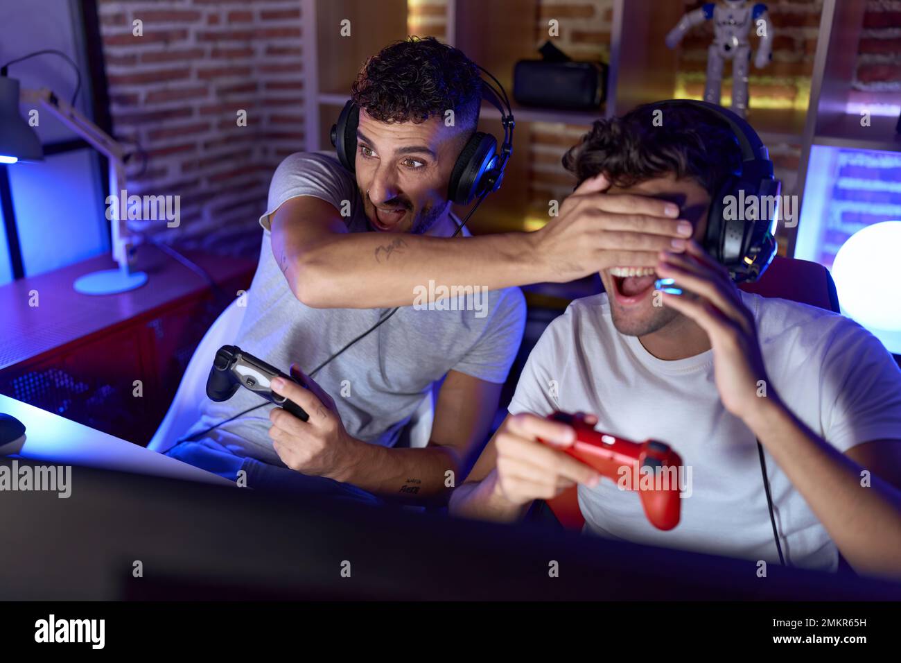 Two hispanic men streamers playing video game covering eyes cheating at ...