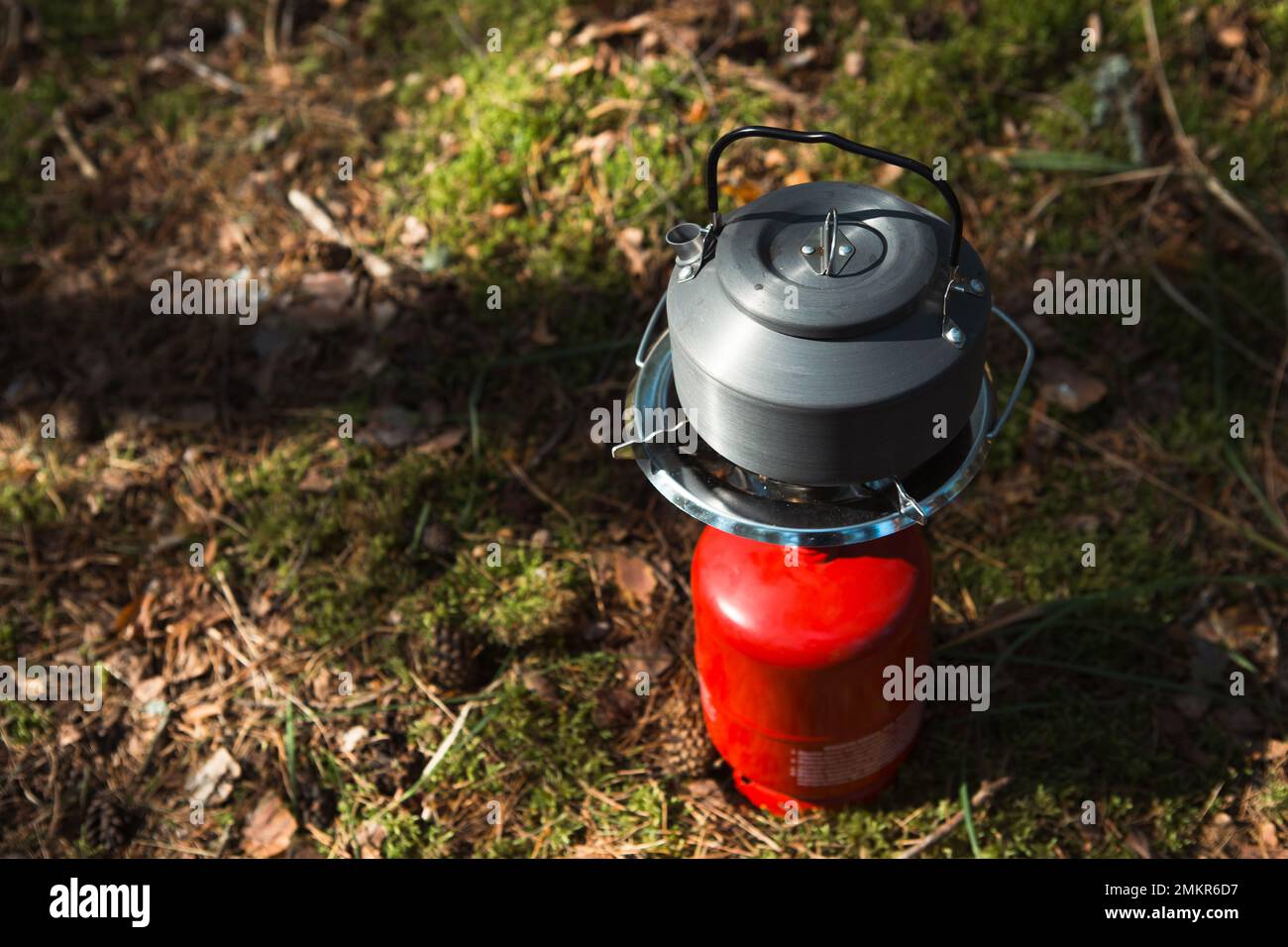Cooking, heating a tourist kettle on a portable gas burner with a red ...
