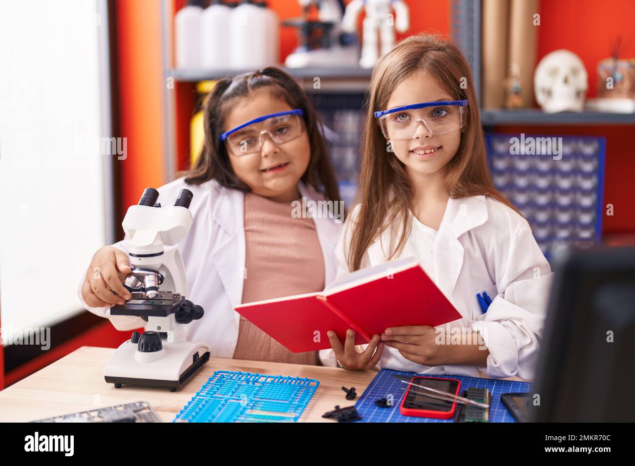 Two kids students using microscope reading notebook at laboratory ...