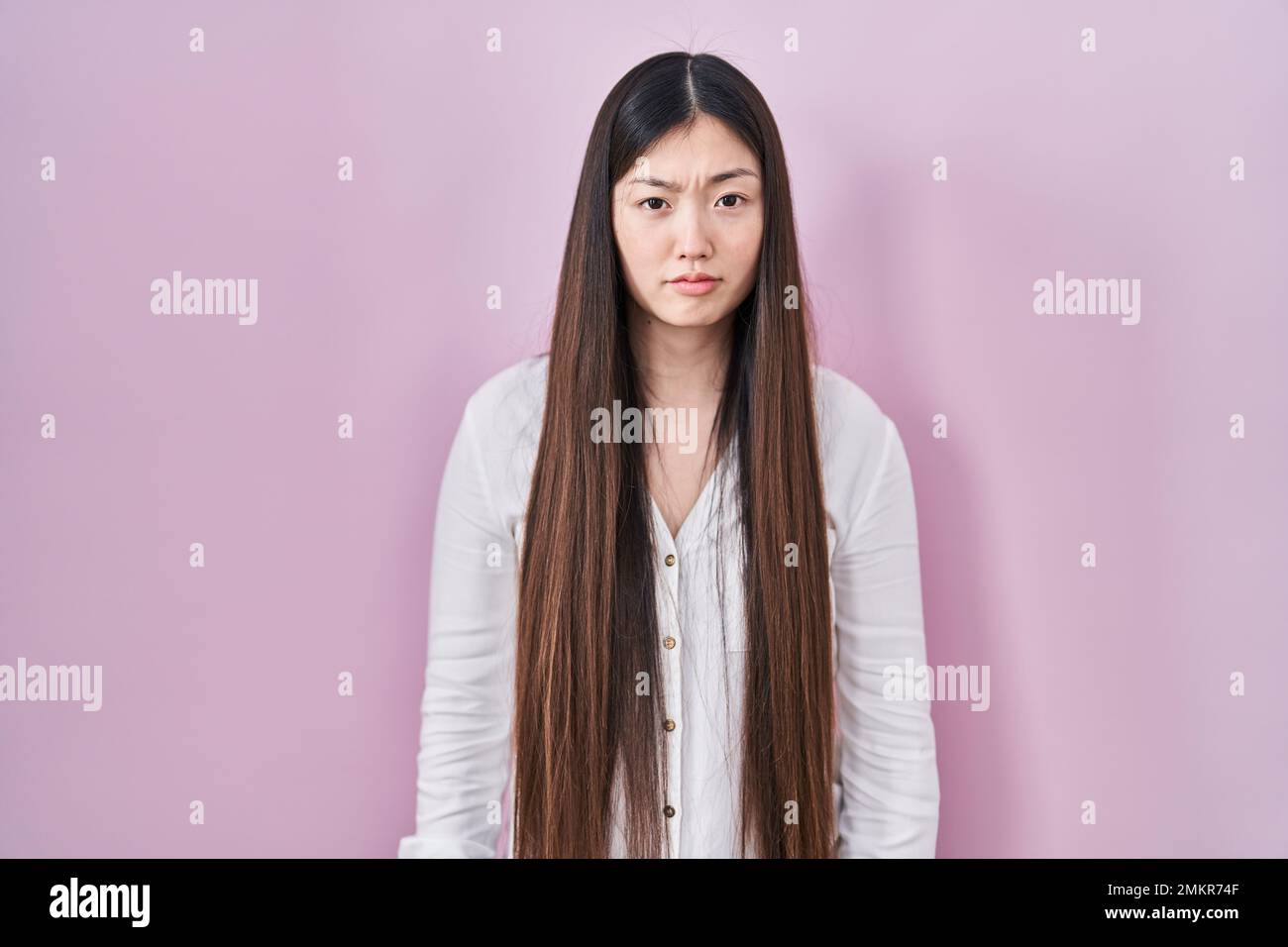 Chinese young woman standing over pink background depressed and worry ...