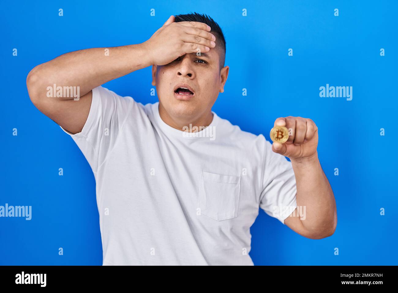 Hispanic young man holding virtual currency bitcoin stressed and ...