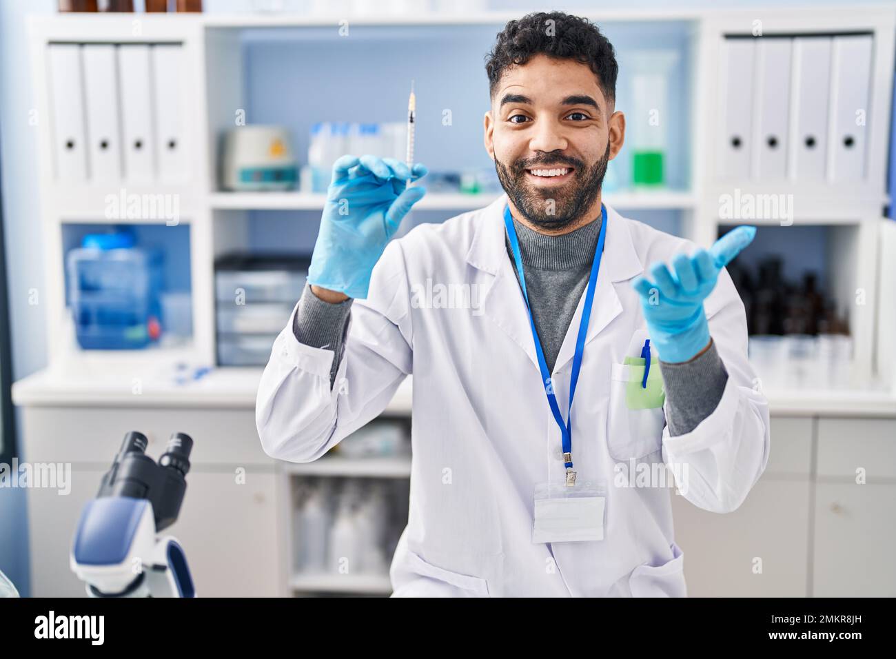 Hispanic man with beard working at scientist laboratory holding syringe ...