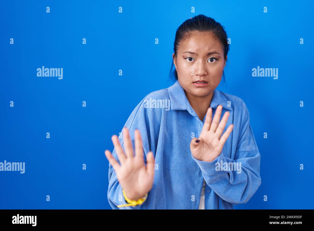 Asian young woman standing over blue background afraid and terrified ...