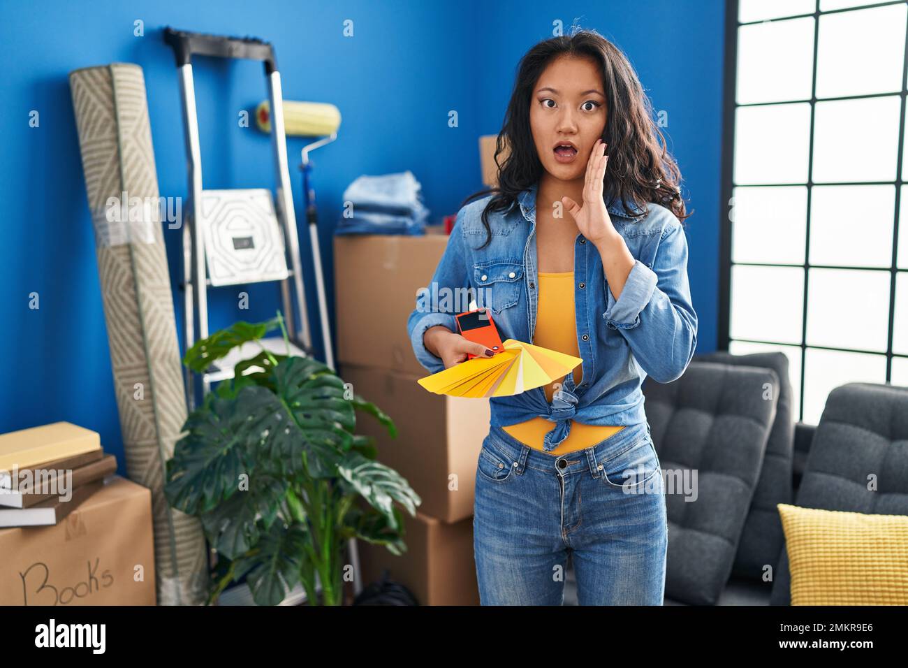 Young asian woman choosing color of new house wall scared and amazed ...