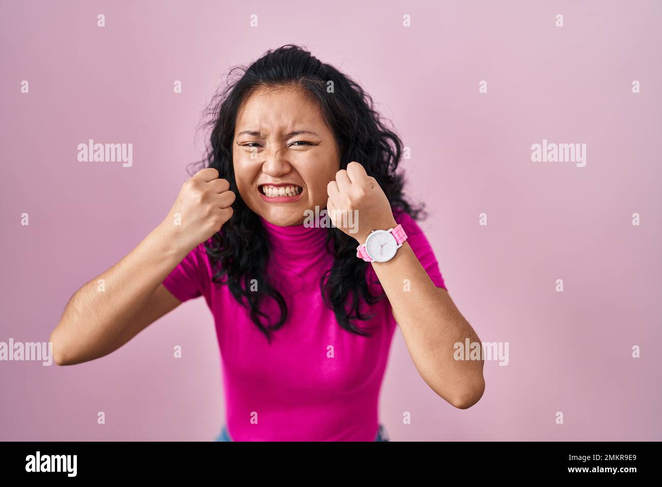 Young asian woman standing over pink background angry and mad raising ...