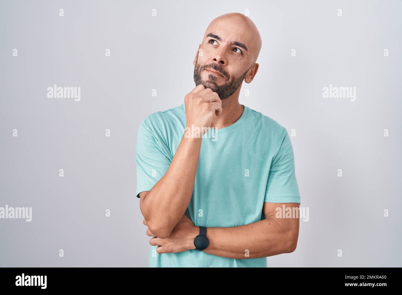 Middle age bald man standing over white background with hand on chin ...