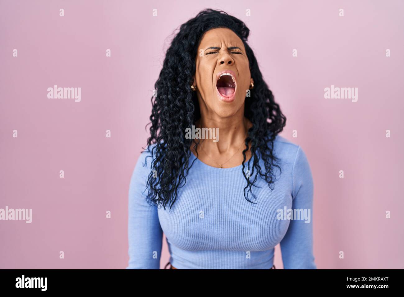 Middle age hispanic woman standing over pink background angry and mad ...
