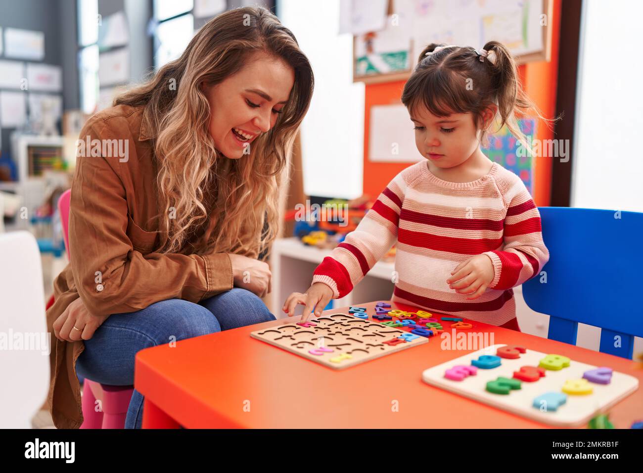 Teacher and toddler playing with maths puzzle game sitting on table at ...
