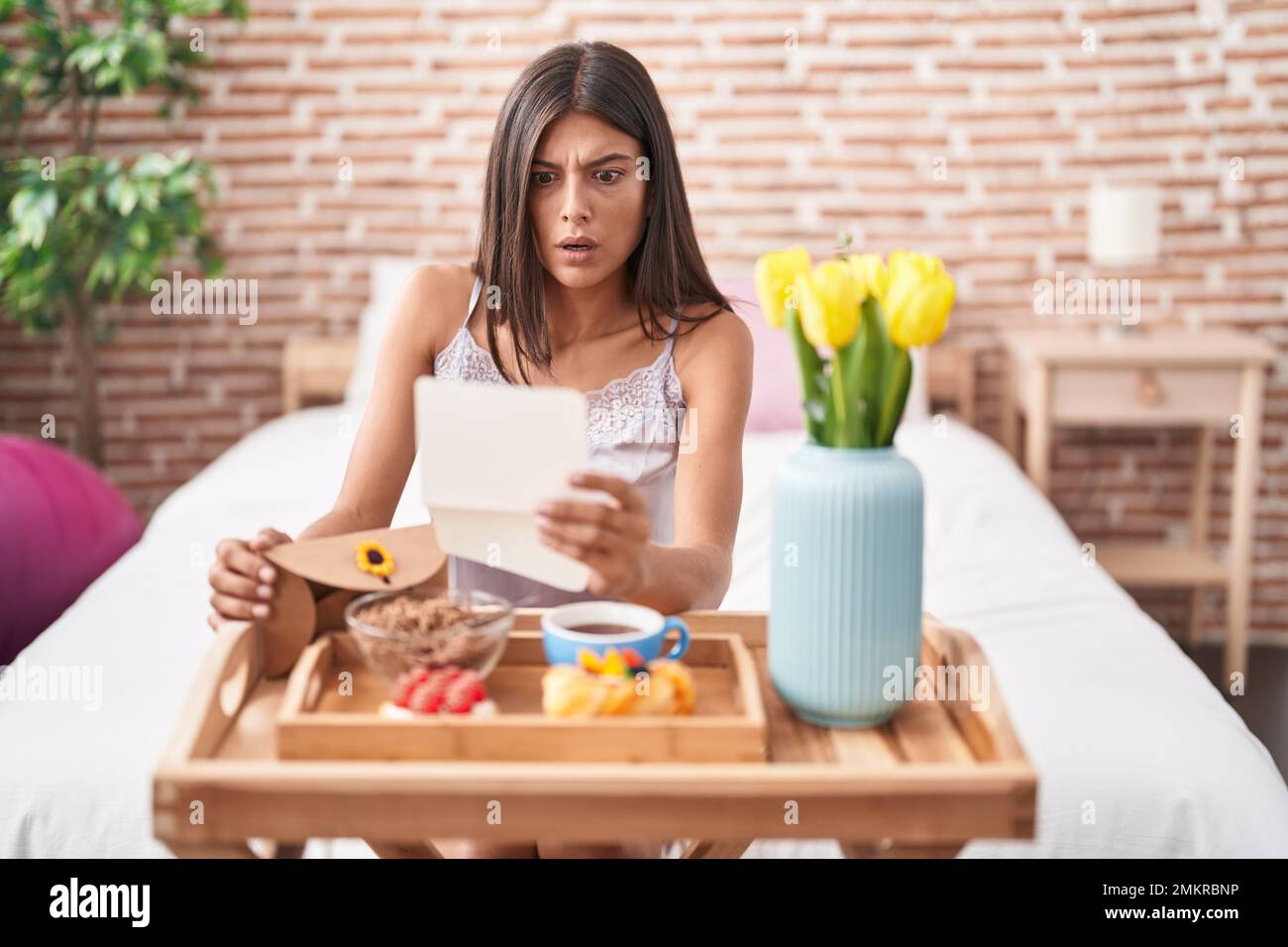 Brunette young woman eating breakfast in the bed reading a letter in ...