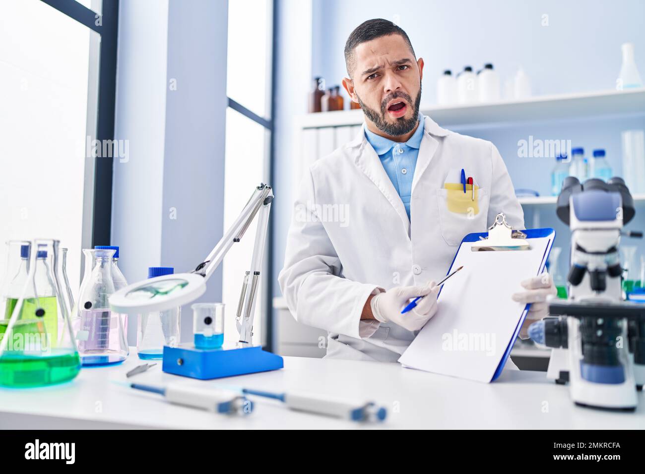 Hispanic man working at scientist laboratory holding blank clipboard in ...
