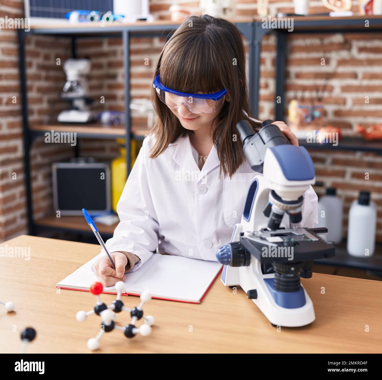 Adorable hispanic girl student using microscope writing on noteboo at ...