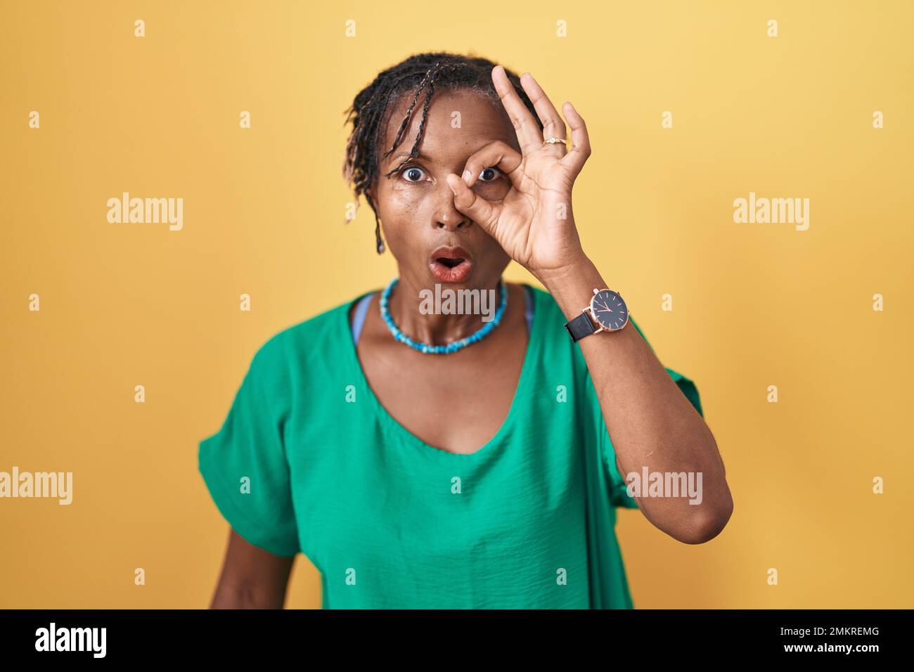 African woman with dreadlocks standing over yellow background doing ok ...