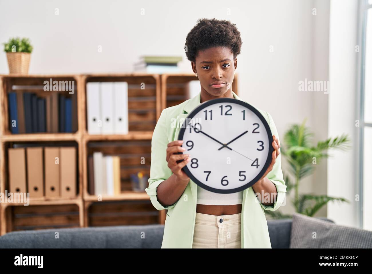 African american woman holding big clock depressed and worry for ...