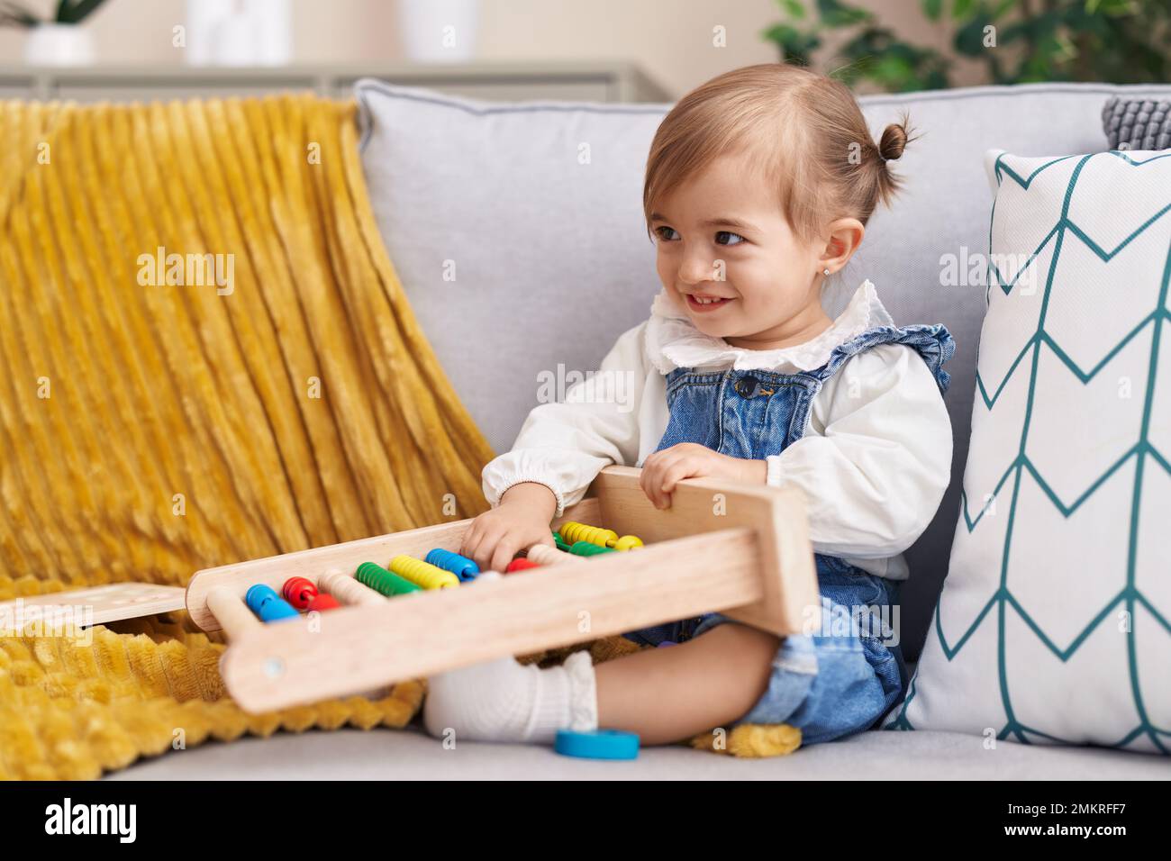 Adorable blonde toddler playing with abacus sitting on sofa at home ...