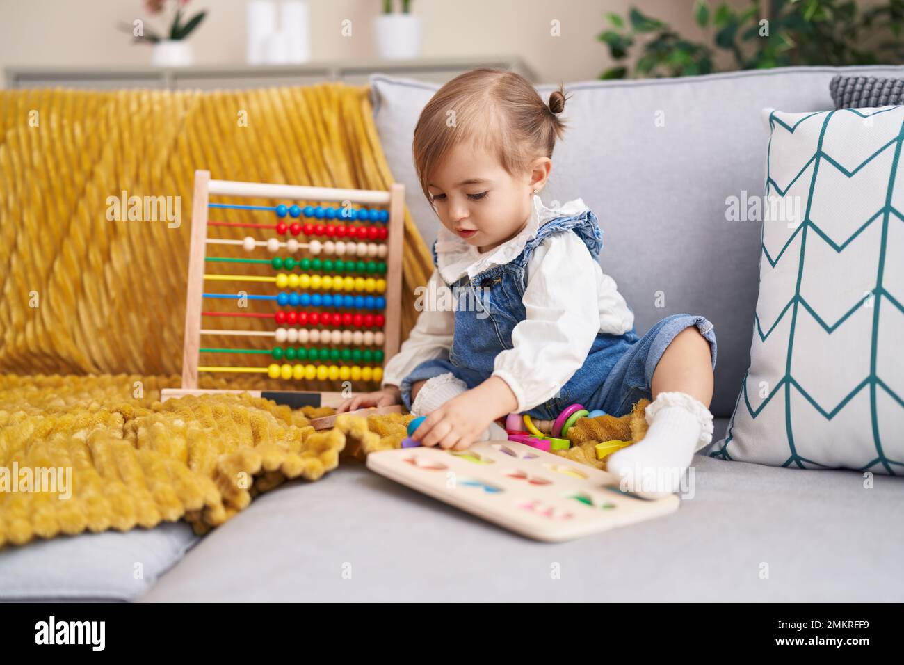 Adorable blonde toddler playing with abacus sitting on sofa at home ...