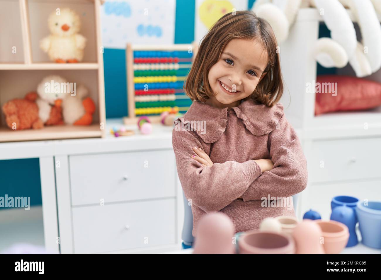 Adorable hispanic girl smiling confident sitting on table with arms crossed gesture at ...