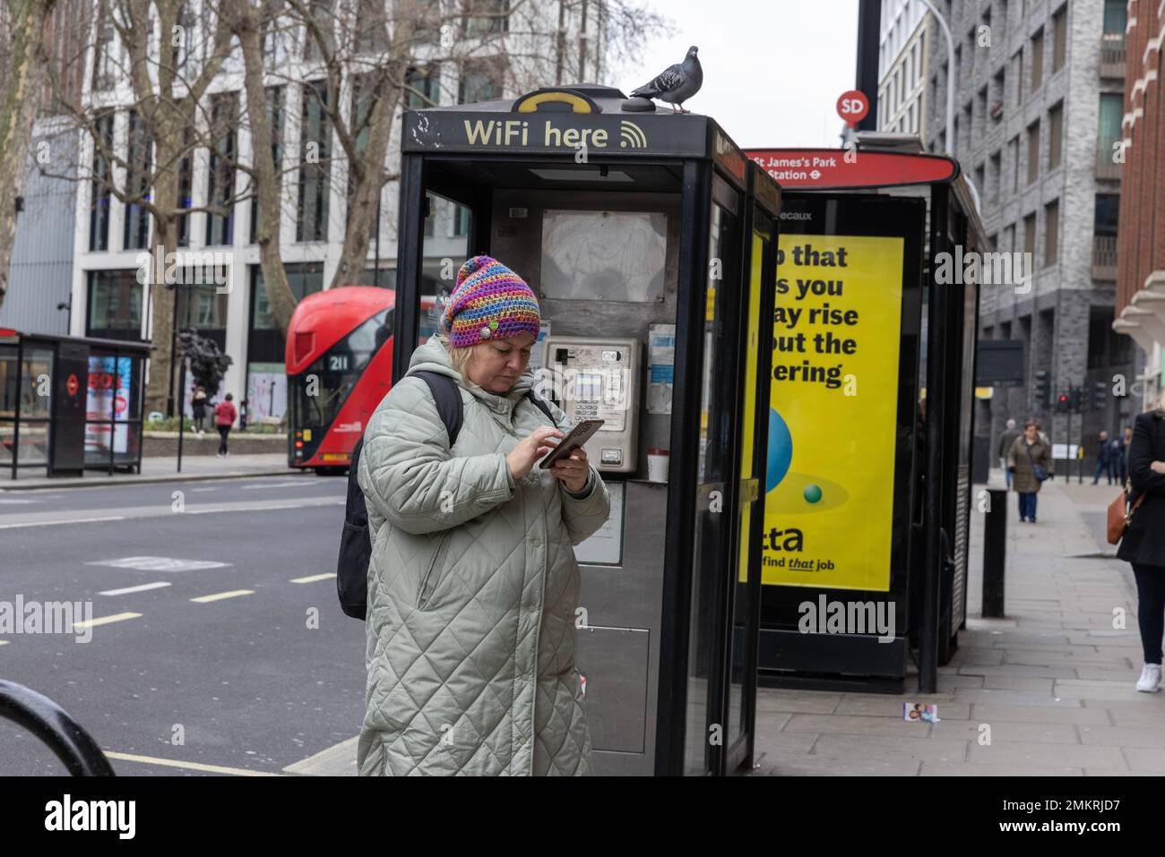 Woman surfing the internet on her smartphone whilst stood next to a ...