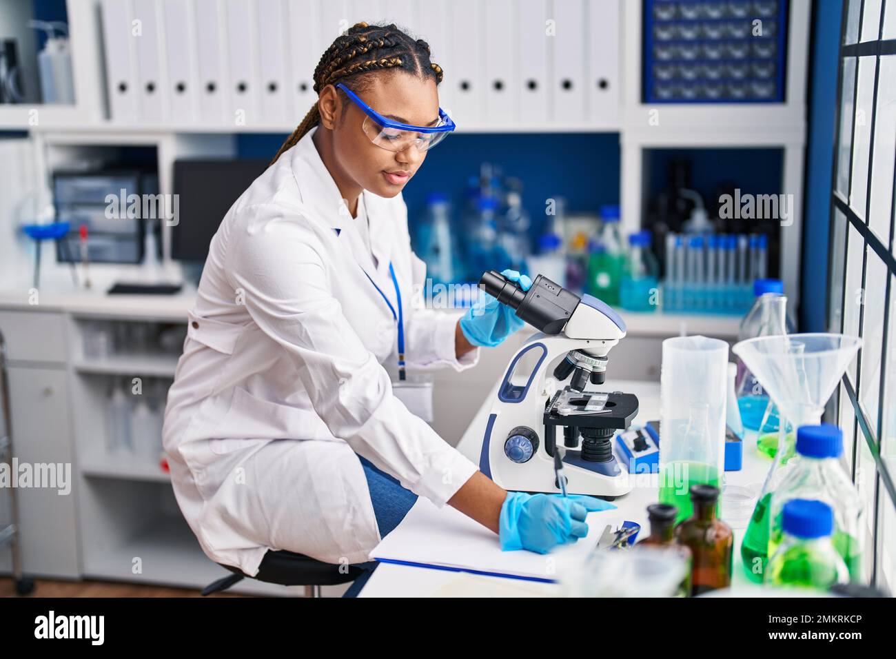African american woman scientist using microscope writing document at laboratory Stock Photo - Alamy