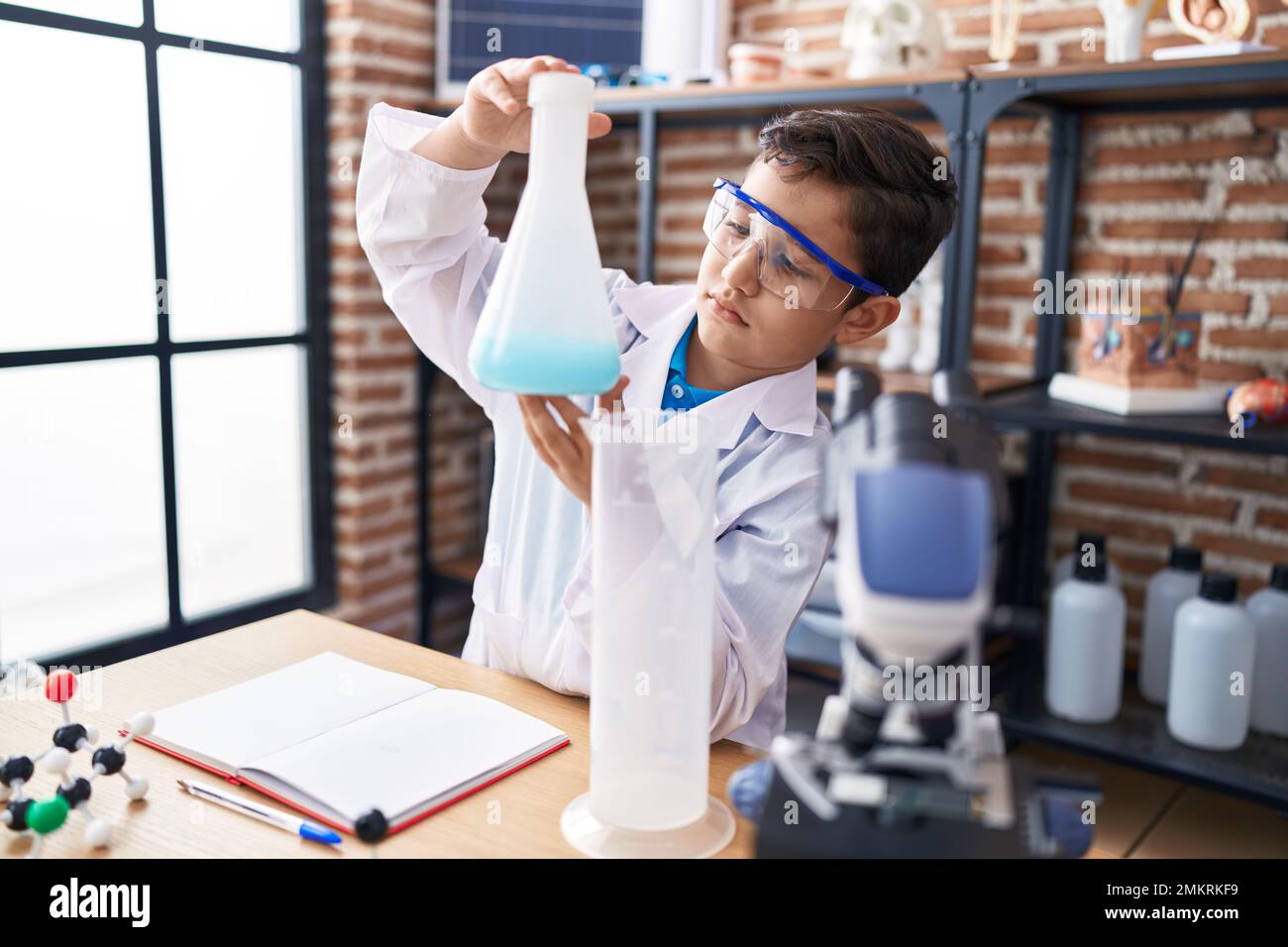 Adorable hispanic boy student holding test tube at laboratory classroom ...
