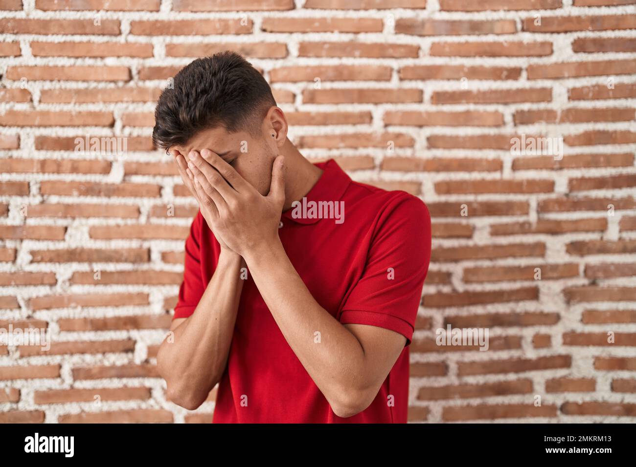 Young hispanic man standing over bricks wall with sad expression ...