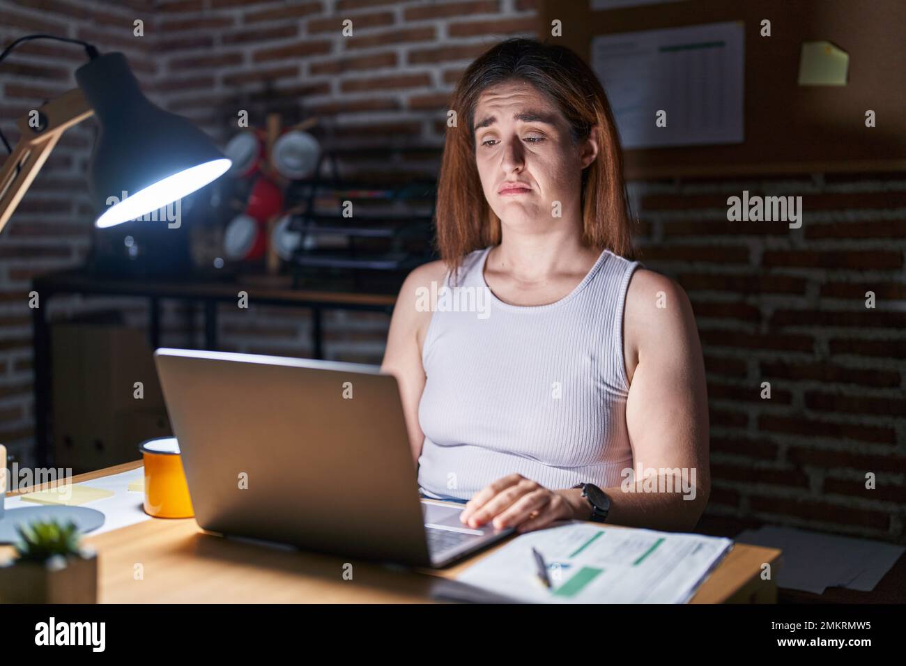 Brunette woman working at the office at night depressed and worry for ...