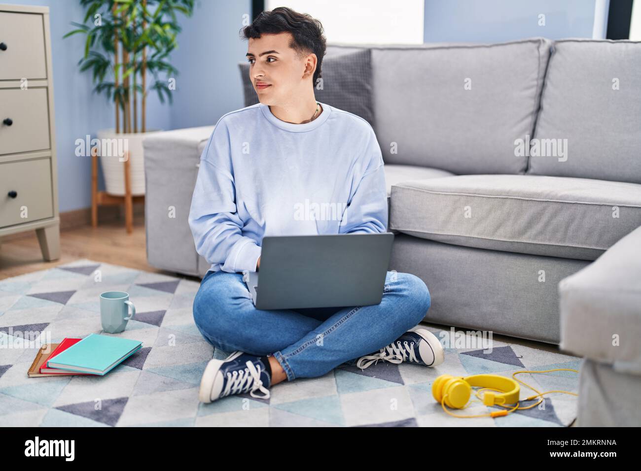 Non binary person studying using computer laptop sitting on the floor looking to side, relax ...