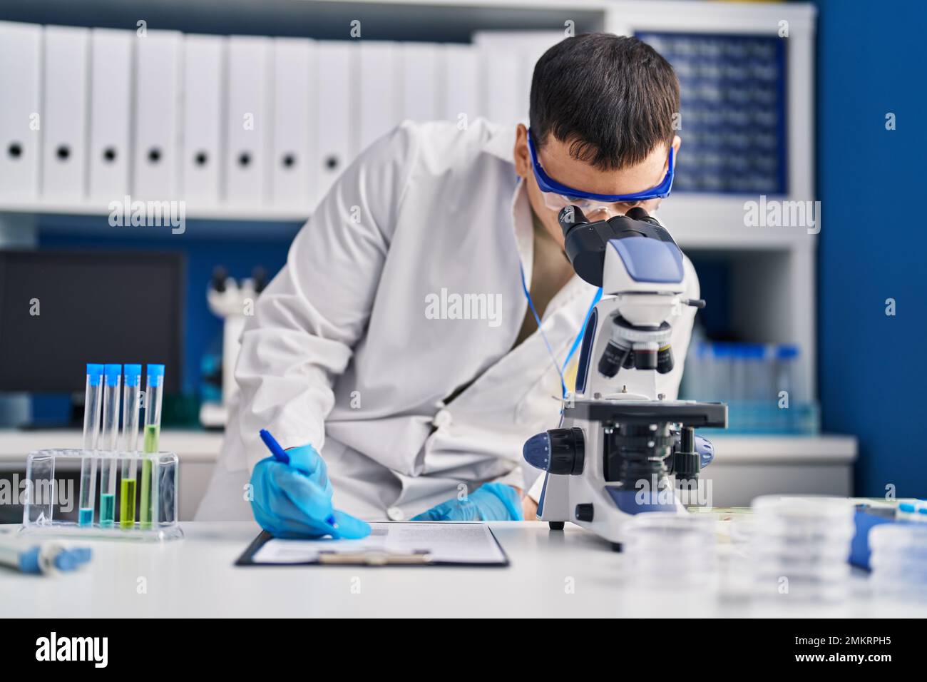 Young man scientist writing on document using mircoscope at laboratory ...