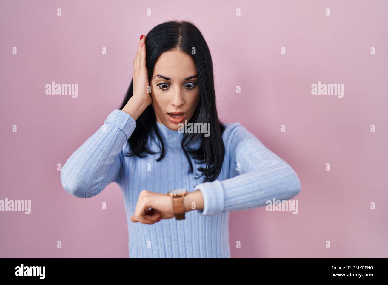 Hispanic woman standing over pink background looking at the watch time ...