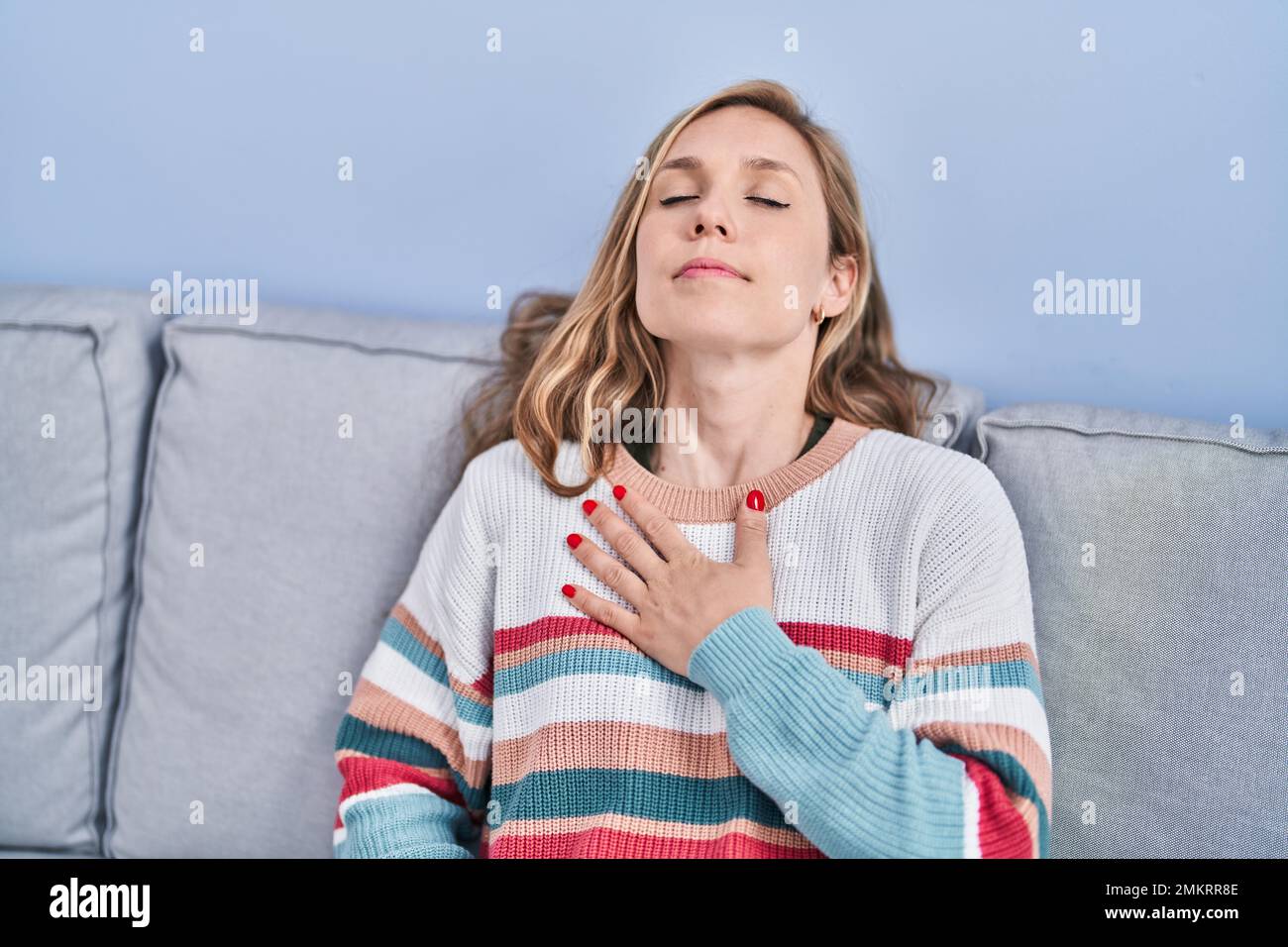 Young blonde woman sitting on sofa suffering heart attack at home Stock ...