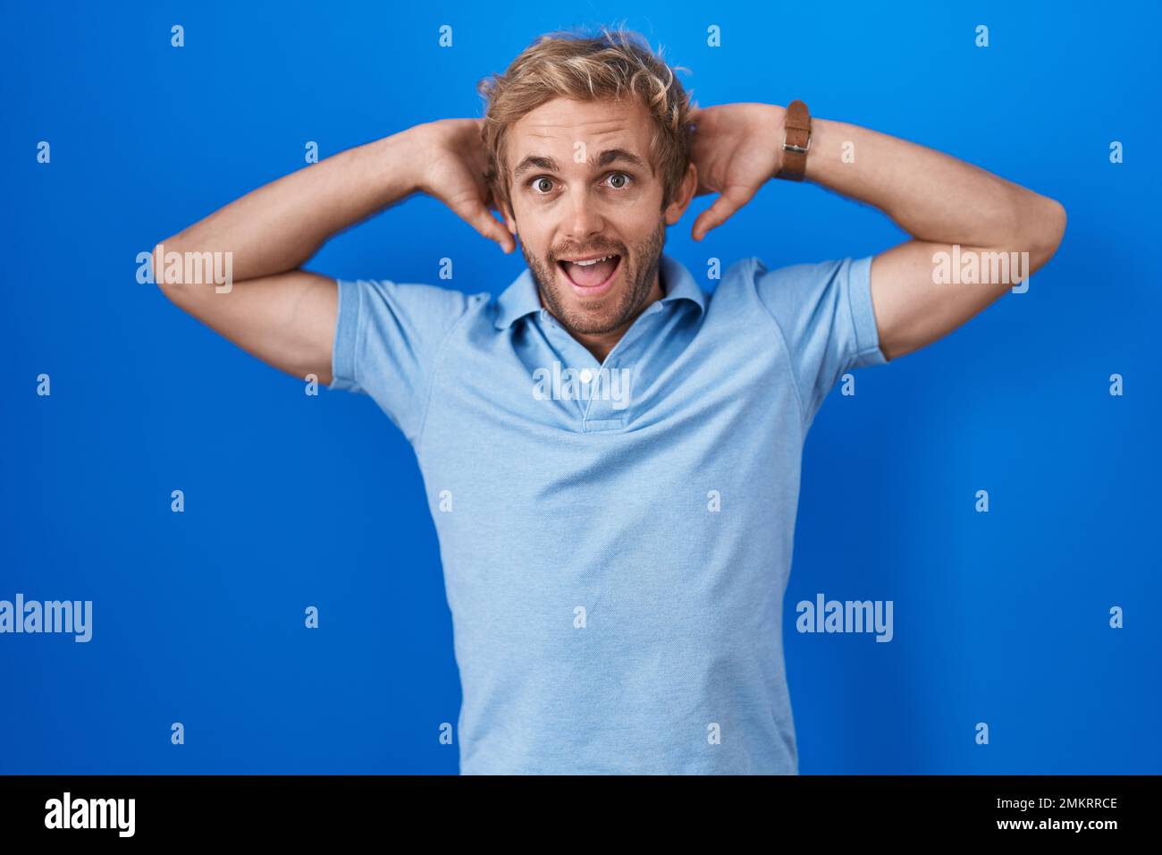 Caucasian man standing over blue background crazy and scared with hands ...