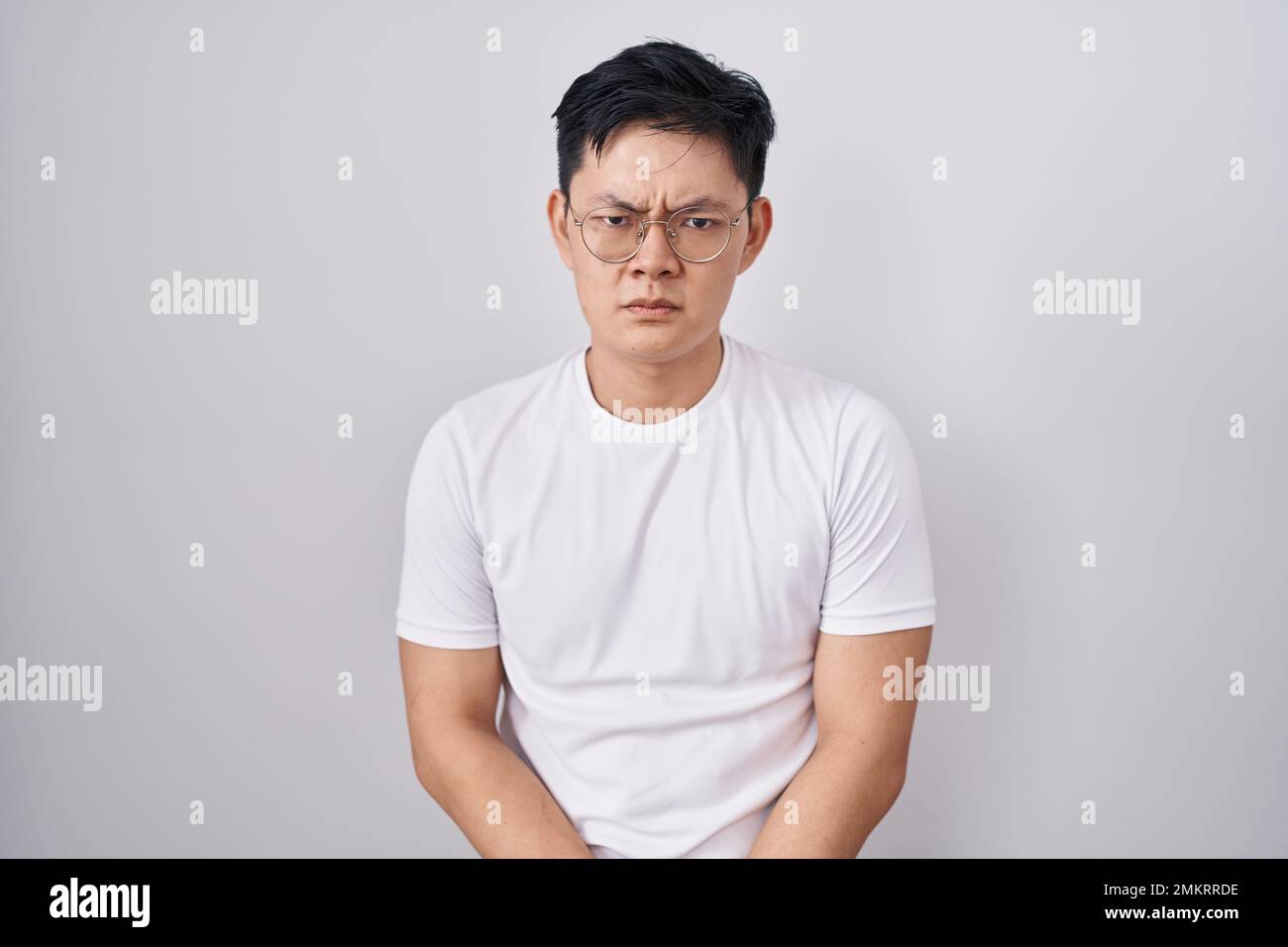 Young asian man standing over white background skeptic and nervous ...