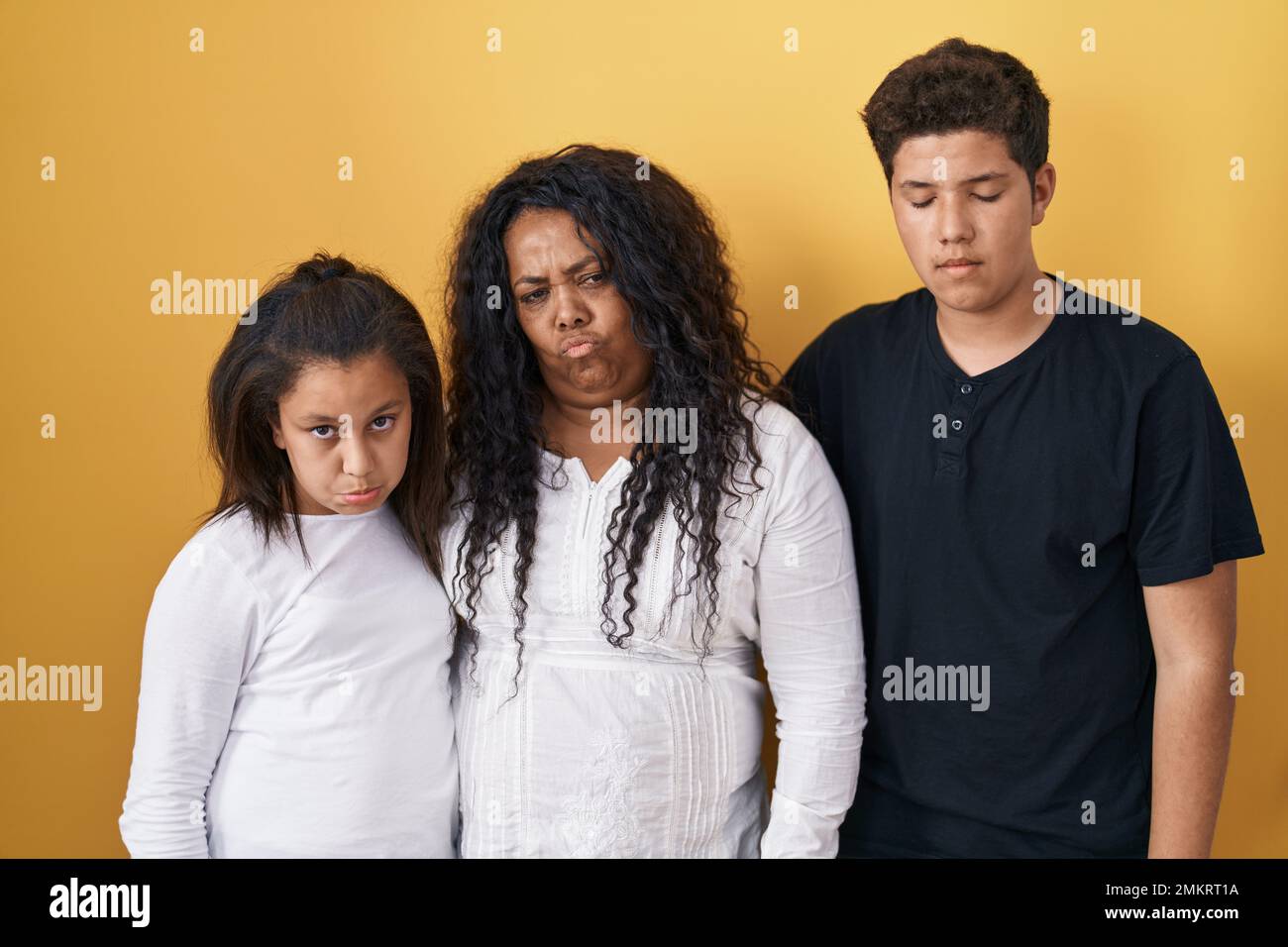 Family of mother, daughter and son standing over yellow background ...