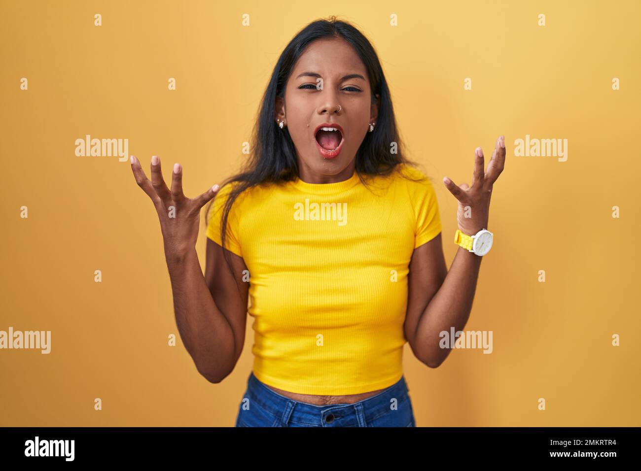 Young indian woman standing over yellow background crazy and mad ...