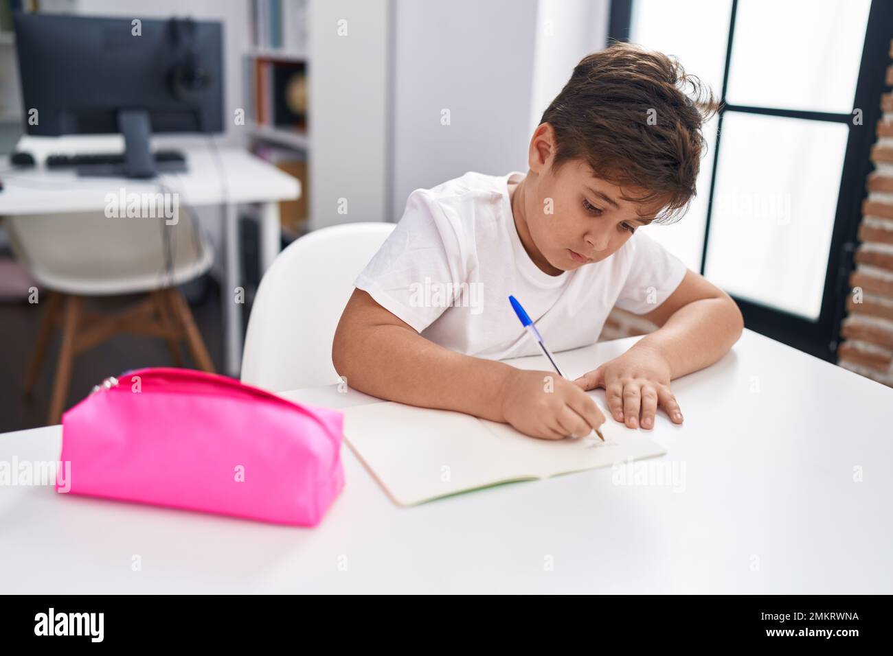 Adorable hispanic boy student writing on notebook at classroom Stock ...