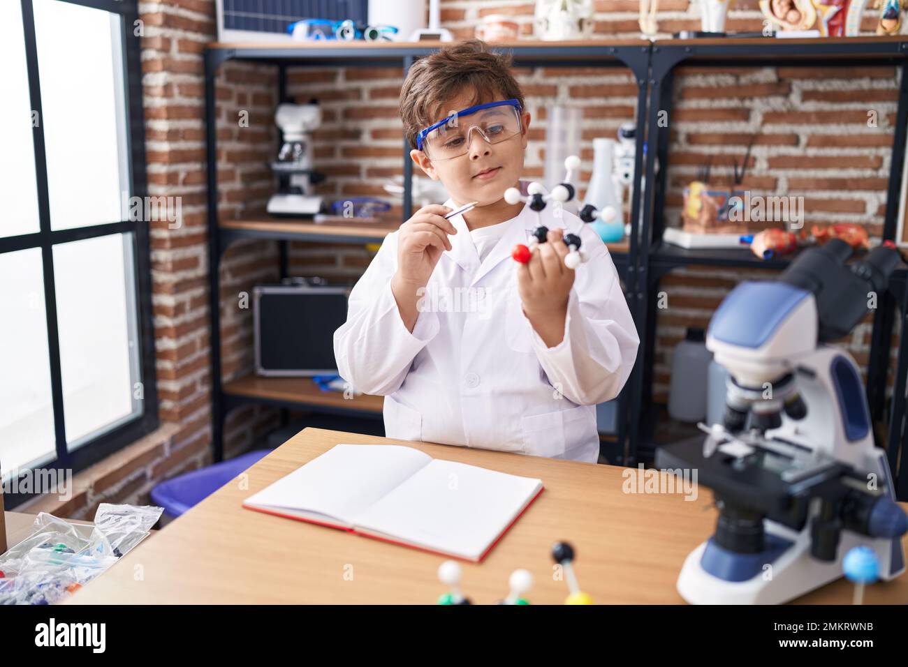 Adorable hispanic boy student looking molecules at laboratory classroom ...