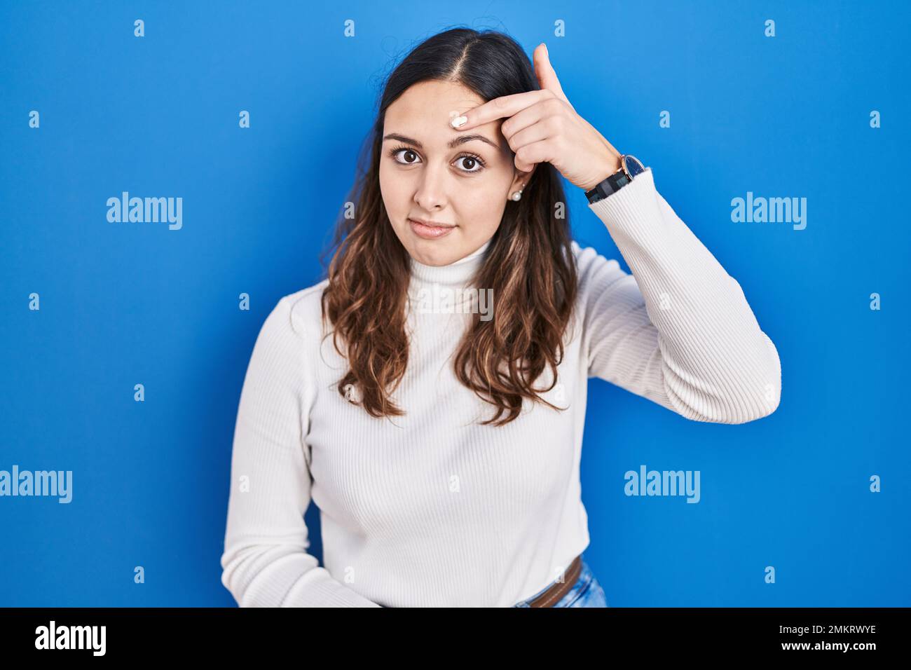 Young hispanic woman standing over blue background pointing unhappy to ...
