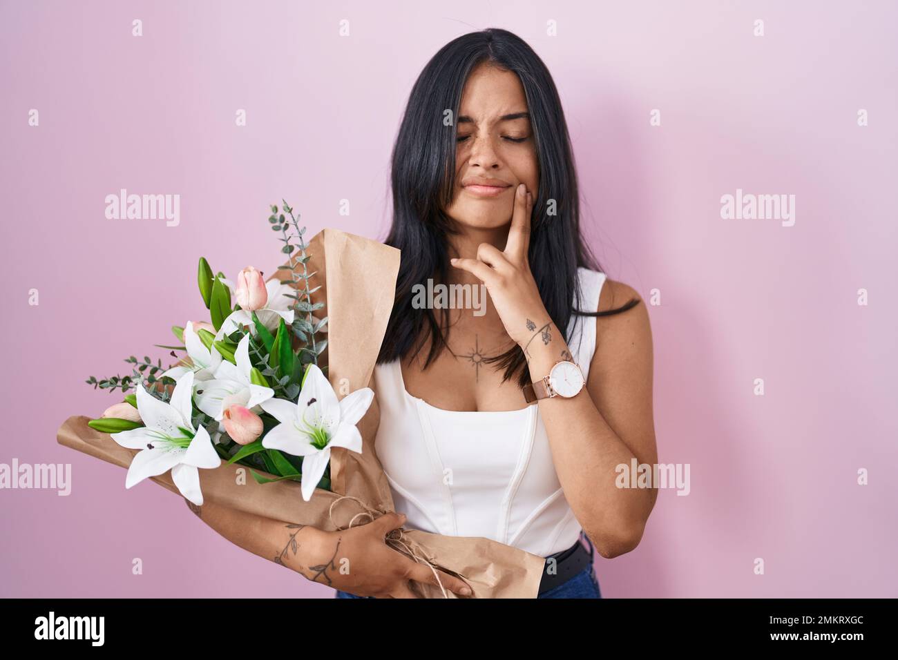 Brunette woman holding bouquet of white flowers touching mouth with ...