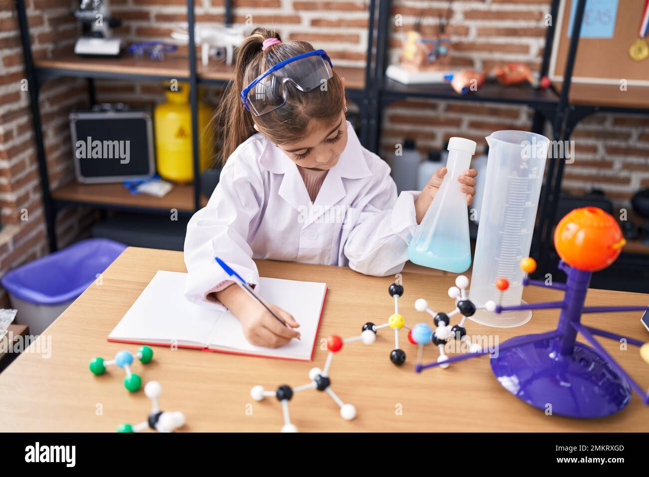 Adorable hispanic girl student holding test tube writing on notebook at ...