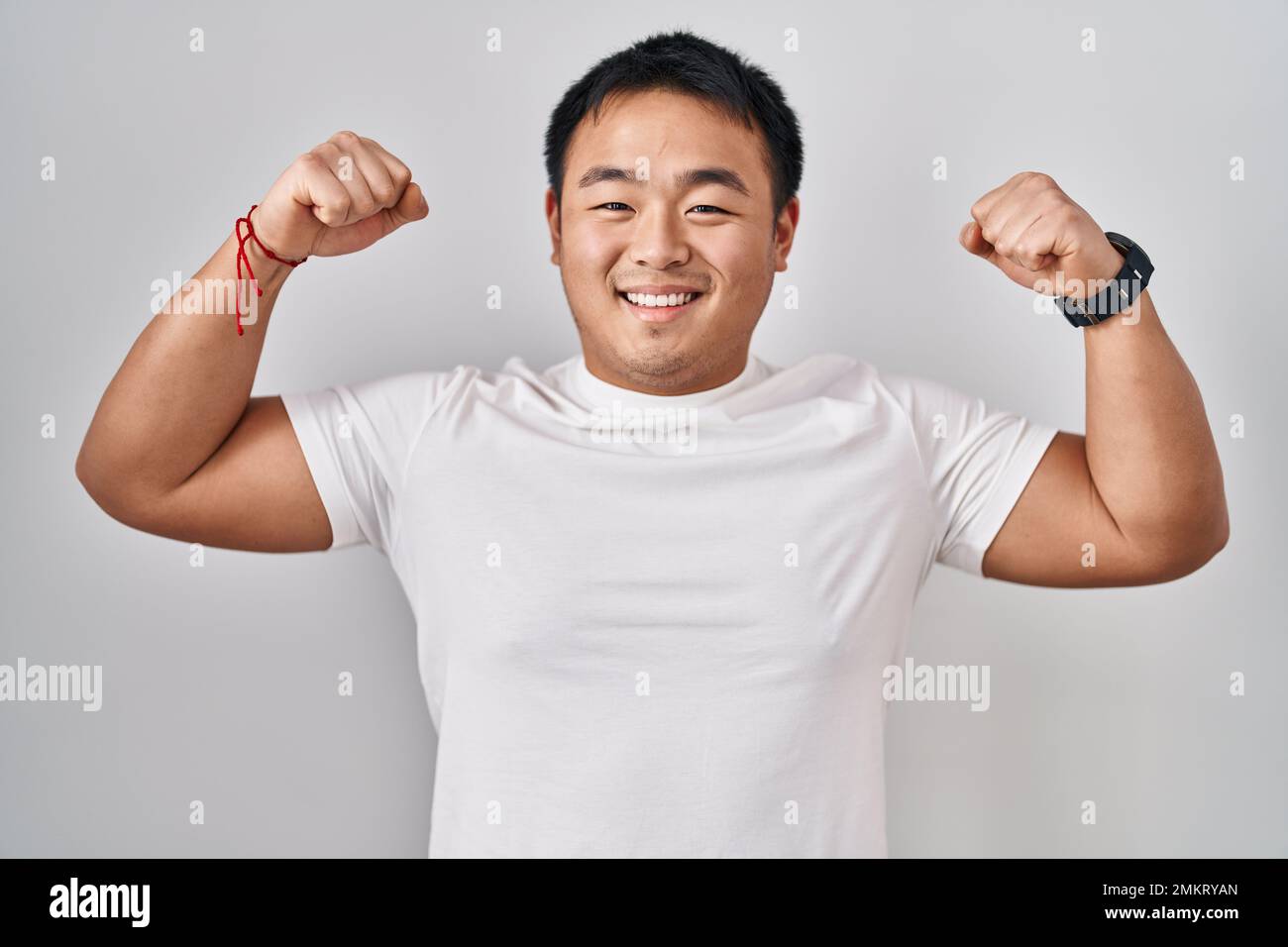 Young chinese man standing over white background showing arms muscles ...