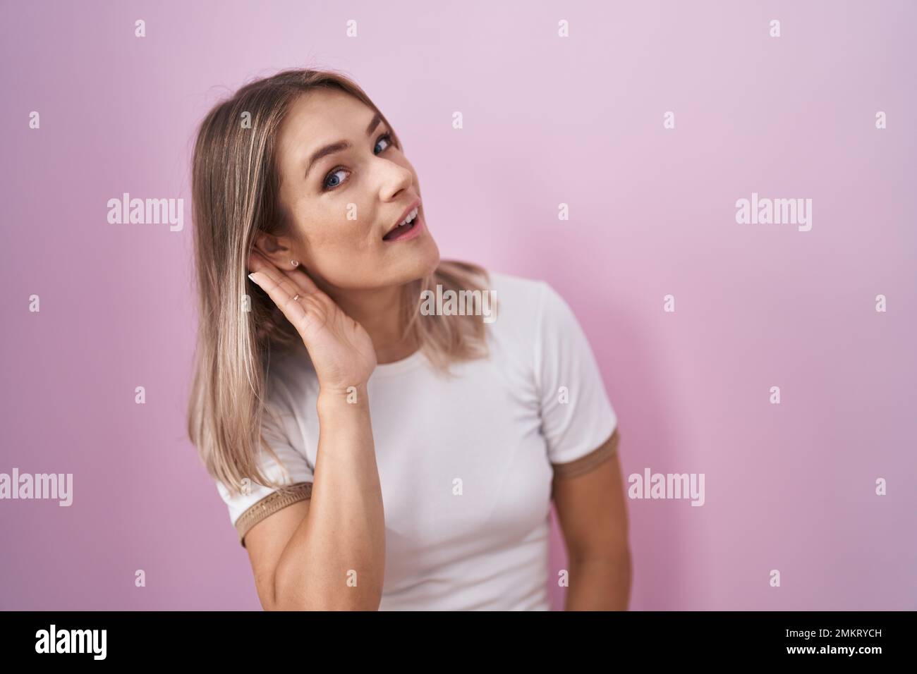 Blonde caucasian woman standing over pink background smiling with hand ...