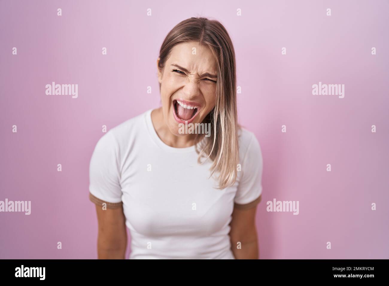 Blonde caucasian woman standing over pink background angry and mad ...