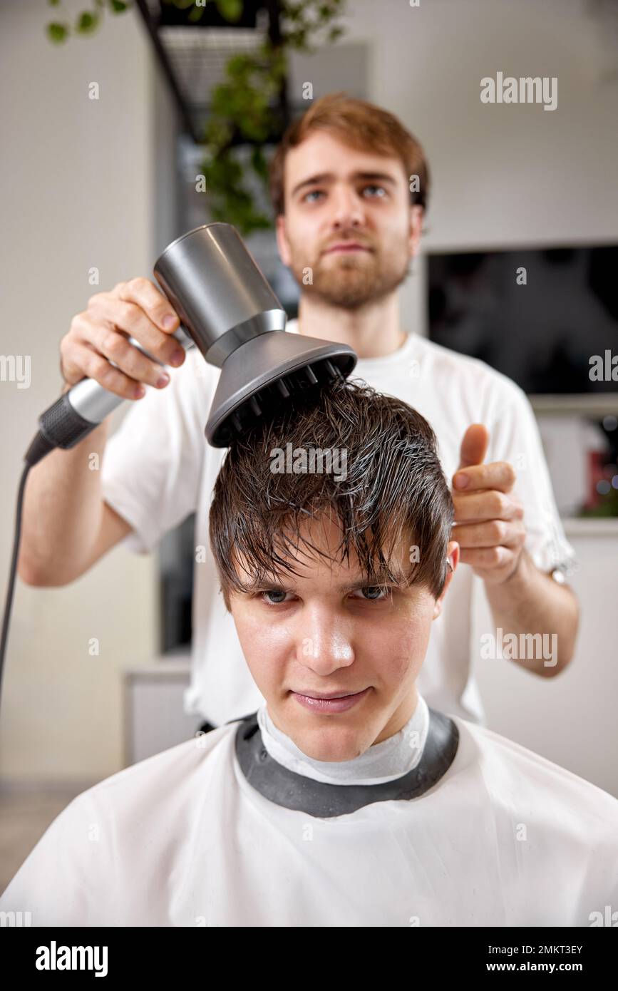 Professional hairdresser during work with man client with hair dryer in ...
