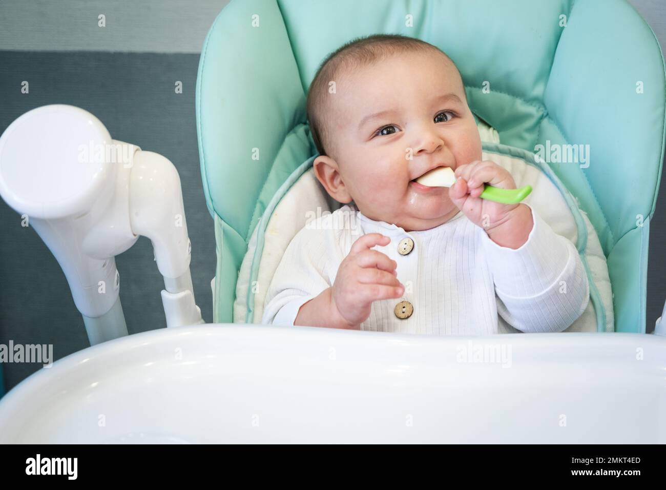 A hungry baby is gnawing on a plastic spoon at the table on a high ...