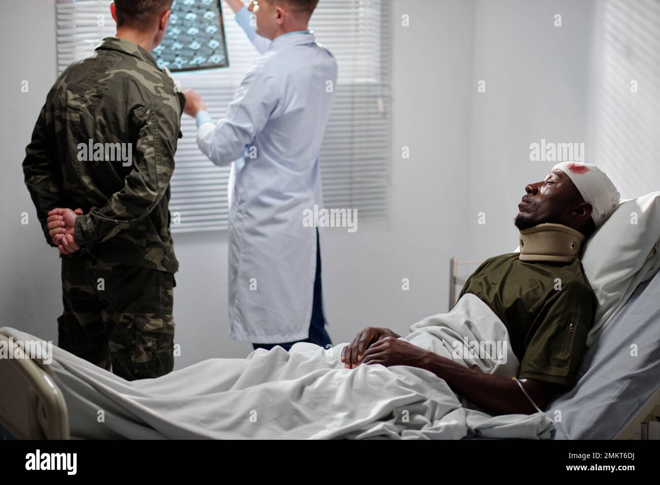 Sick military man with bleeding wound in head looking at doctor talking ...