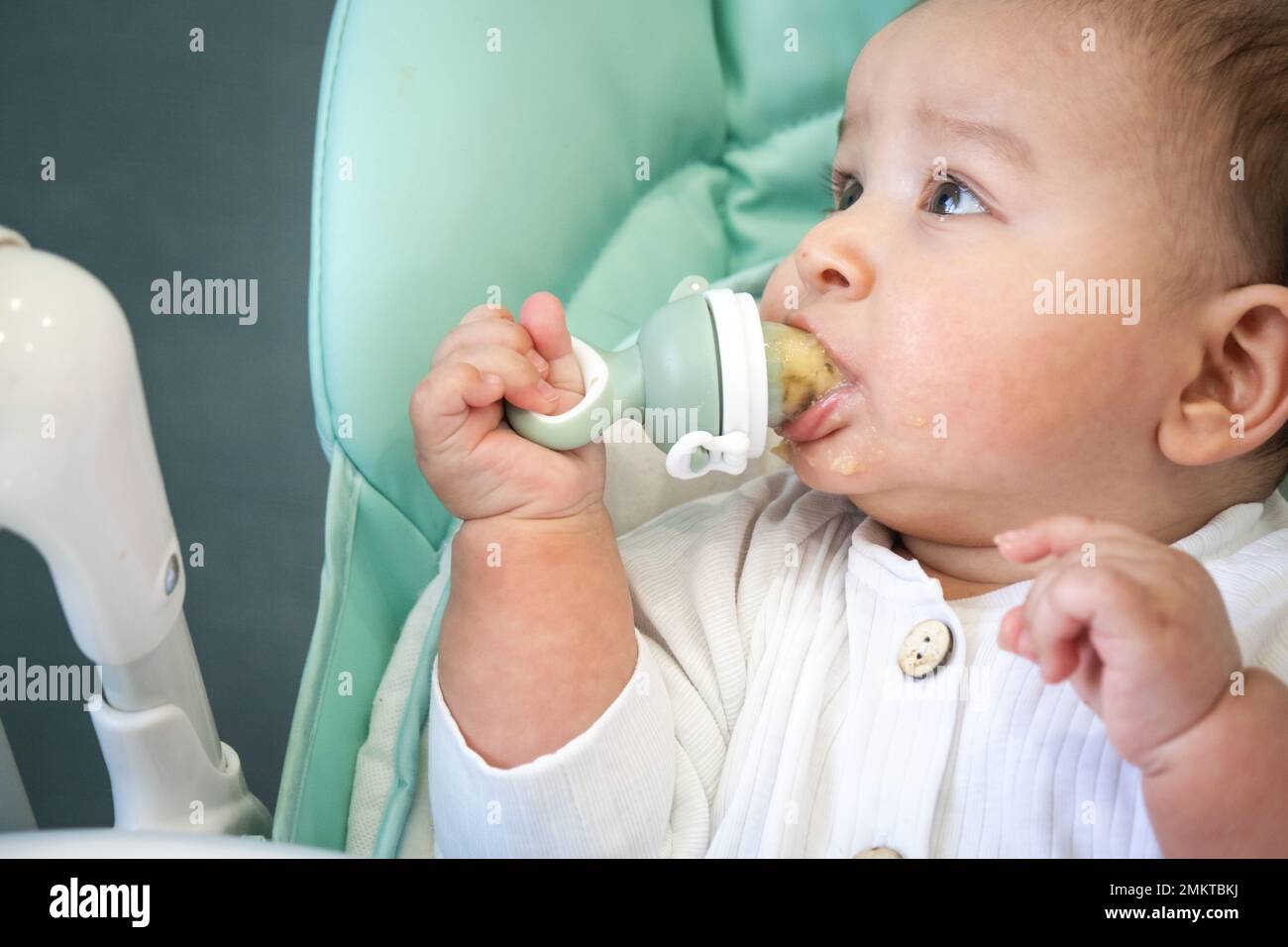 A happy and contented baby eats banana puree from a nipple ...