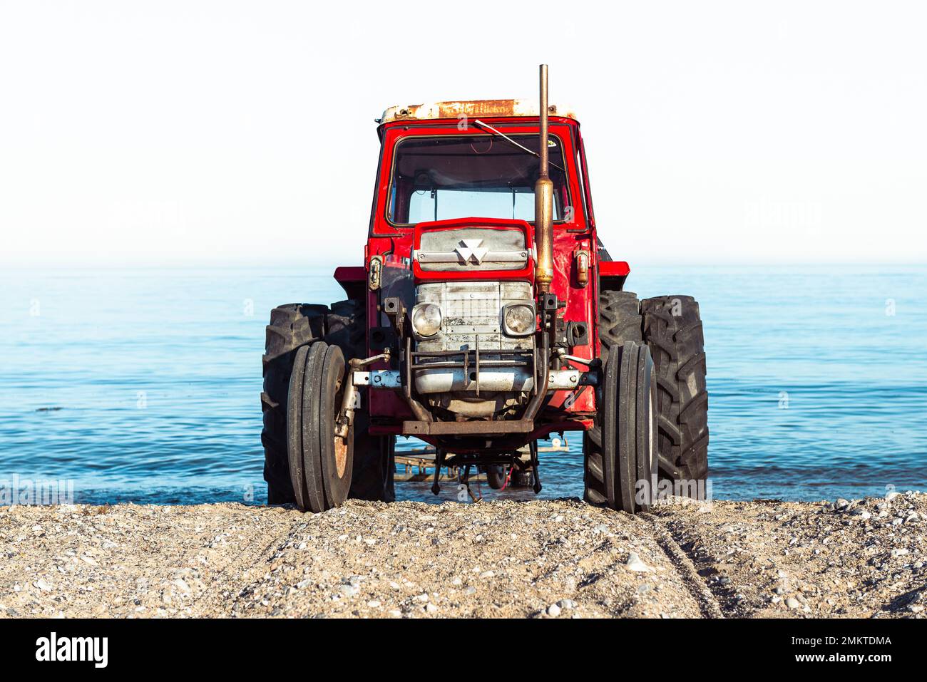 An old, red Massey-Ferguson MF 135 tractor stands with an empty boat ...