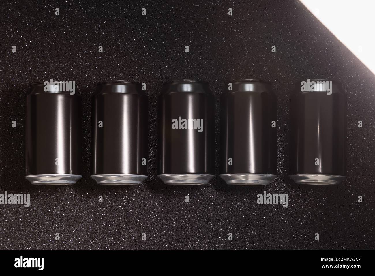 Five black aluminium soda cans in a row with hard lighting from the top ...